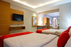 Quarto de hotel com duas camas, televisão, espelho e banheiro visível por uma porta aberta.