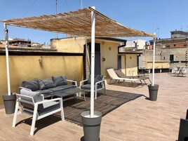 Um pátio externo com um sofá, cadeiras e um toldo.