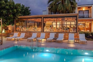 Piscina com espreguiçadeiras e um bar com mesas e cadeiras.