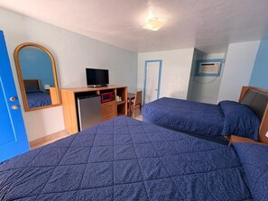 Quarto com duas camas, uma escrivaninha com televisão, micro-ondas e porta com moldura azul.