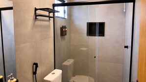 Uma casa de banho moderna com chuveiro de cabine de vidro, sanita e lavatório com dispensador de sabão.