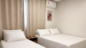 Quarto de hotel com duas camas de solteiro, mesa de cabeceira, aparelho de ar condicionado e quadro na parede.