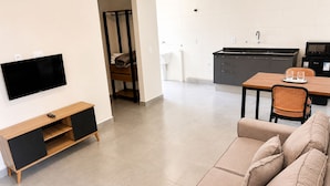 Uma sala de estar moderna com televisão de tela plana, sofá, mesa de jantar com cadeiras e cozinha com micro-ondas e armários.