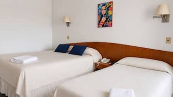 Quarto de hotel com duas camas, cabeceira de madeira, mesa de cabeceira com abajur, telefone e uma obra de arte colorida na parede.