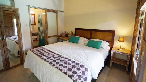 Quarto com uma cama grande, cabeceira de madeira, mesa de cabeceira com abajur e um espelho.
