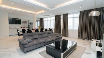 Uma sala de estar moderna com um sofá cinza, uma mesa de centro preta e um espaço de jantar com mesa e cadeiras.