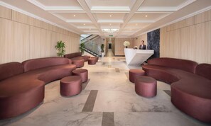 Um saguão de hotel com balcão de recepção, escada e áreas de estar.