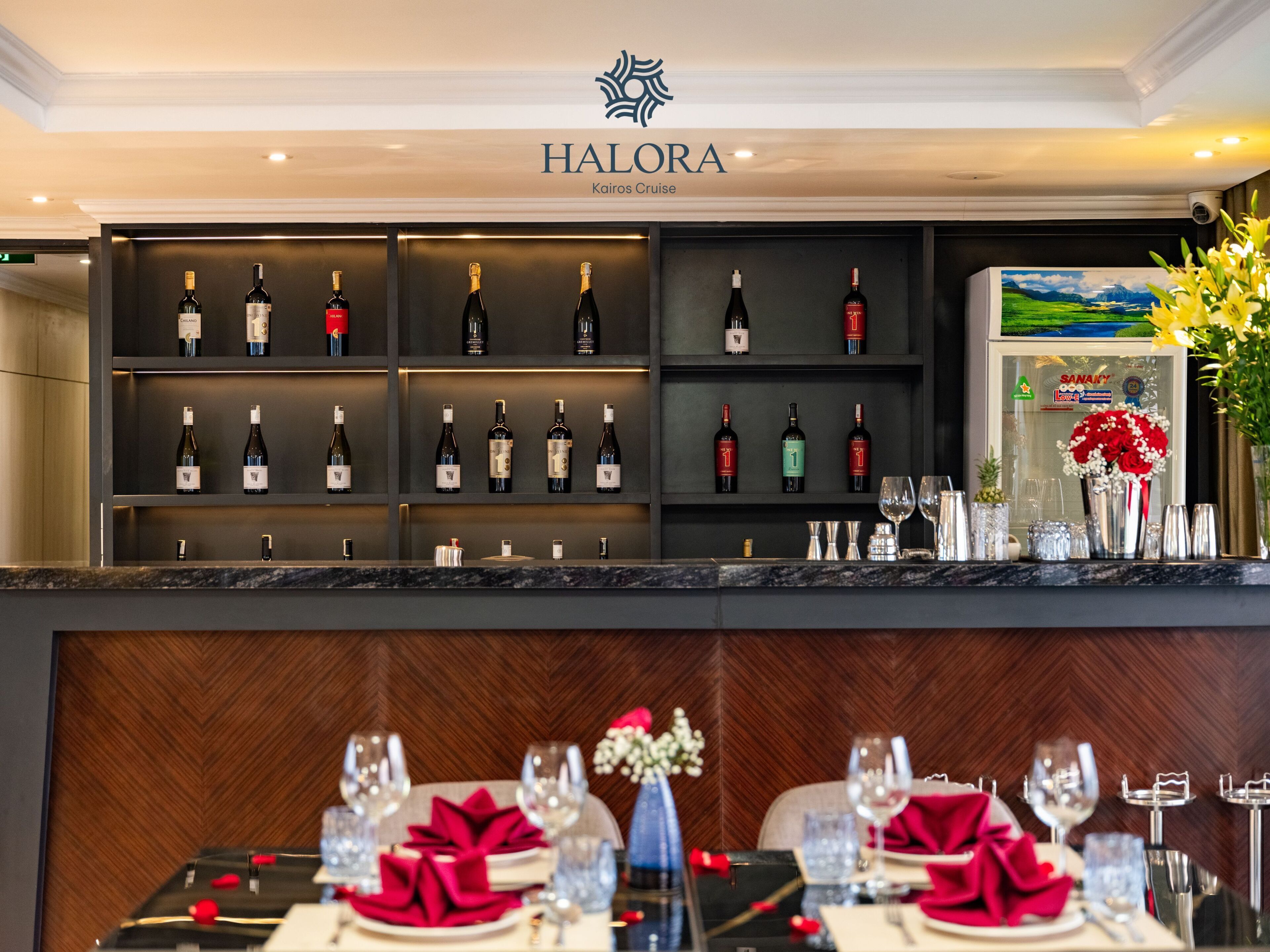 Uma área de bar com várias prateleiras de garrafas de vinho, um balcão com copos e uma sala de jantar com mesas arrumadas.