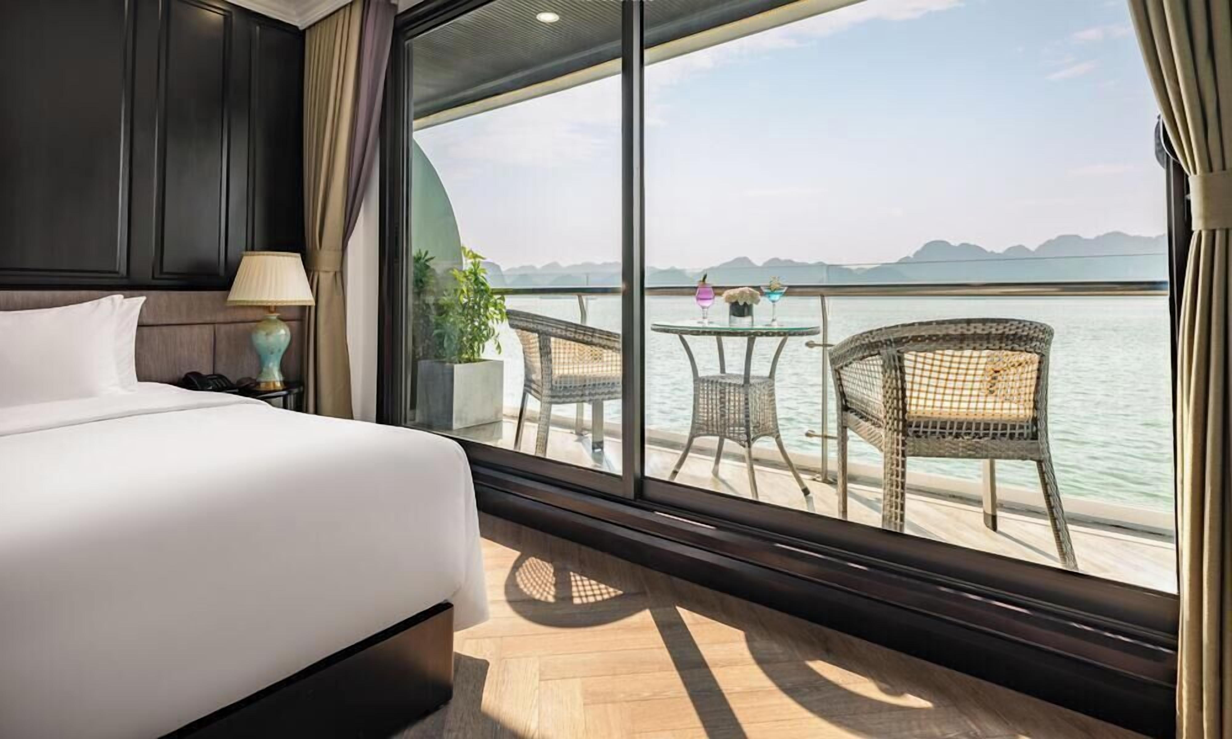 Quarto de hotel com uma janela grande, uma cama, mesa de cabeceira, abajur e vista para a água.
