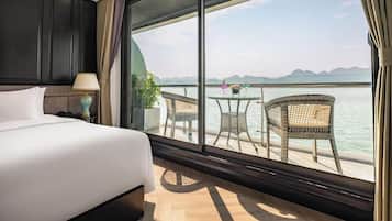 Quarto de hotel com uma janela grande, uma cama, mesa de cabeceira, abajur e vista para a água.