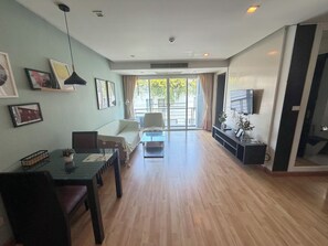 Uma sala de estar moderna com área de jantar, um sofá, uma televisão e uma varanda com cortinas.