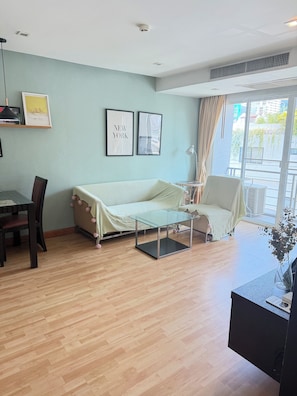 Uma sala de estar com um sofá, uma mesa de centro de vidro, uma mesa de jantar com cadeiras e quadros nas paredes.