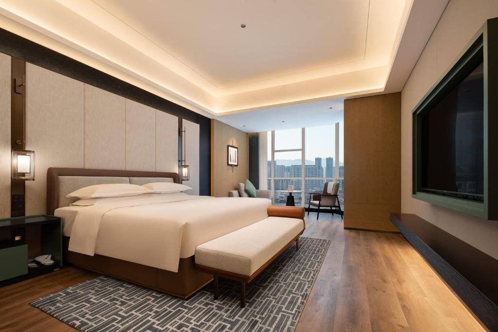 Quarto de hotel moderno com uma cama grande, área de estar e vista para a cidade.