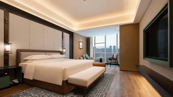 Quarto de hotel moderno com uma cama grande, área de estar e vista para a cidade.