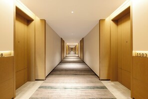Corredor de hotel com portas de madeira, placas de quarto numeradas e piso coberto por carpete.