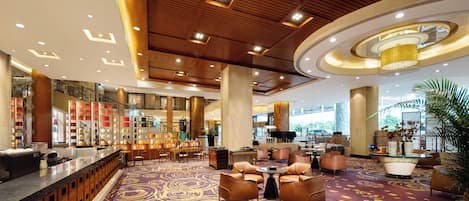 Um hall de hotel com área de estar central, balcão de recepção e uma grande janela com vista para o exterior.