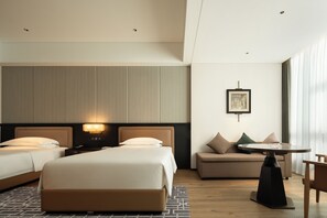 Quarto de hotel com duas camas, um sofá, uma mesinha e um quadro na parede.