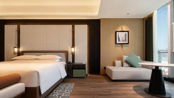 Quarto de hotel moderno com uma cama grande, área de estar com uma mesa e vista para a cidade pela janela.
