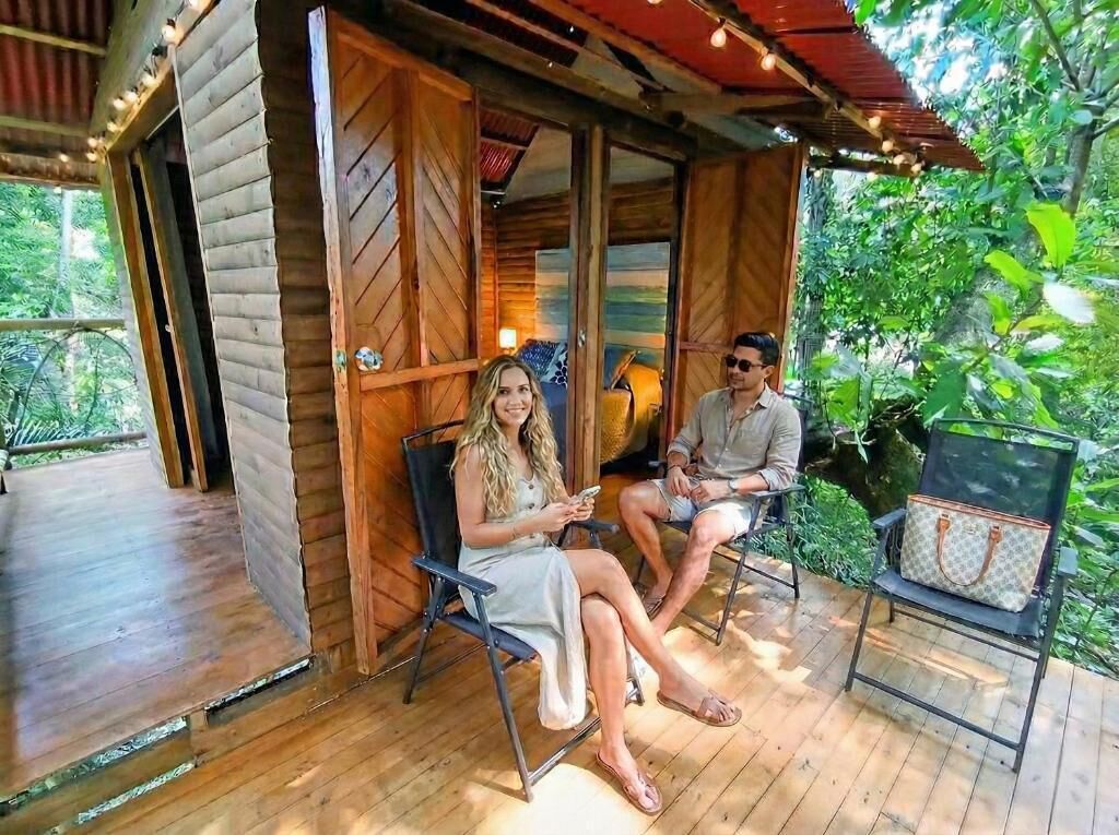 Uma cabana de madeira com varanda, duas cadeiras e uma bolsa em um banco.