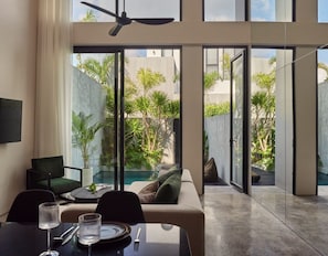 Sala moderna com porta de vidro para área da piscina, ventilador de teto e mesa de jantar posta com copos e talheres.