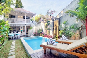 Uma área de piscina com espreguiçadeiras, uma escadaria e um edifício com varanda.