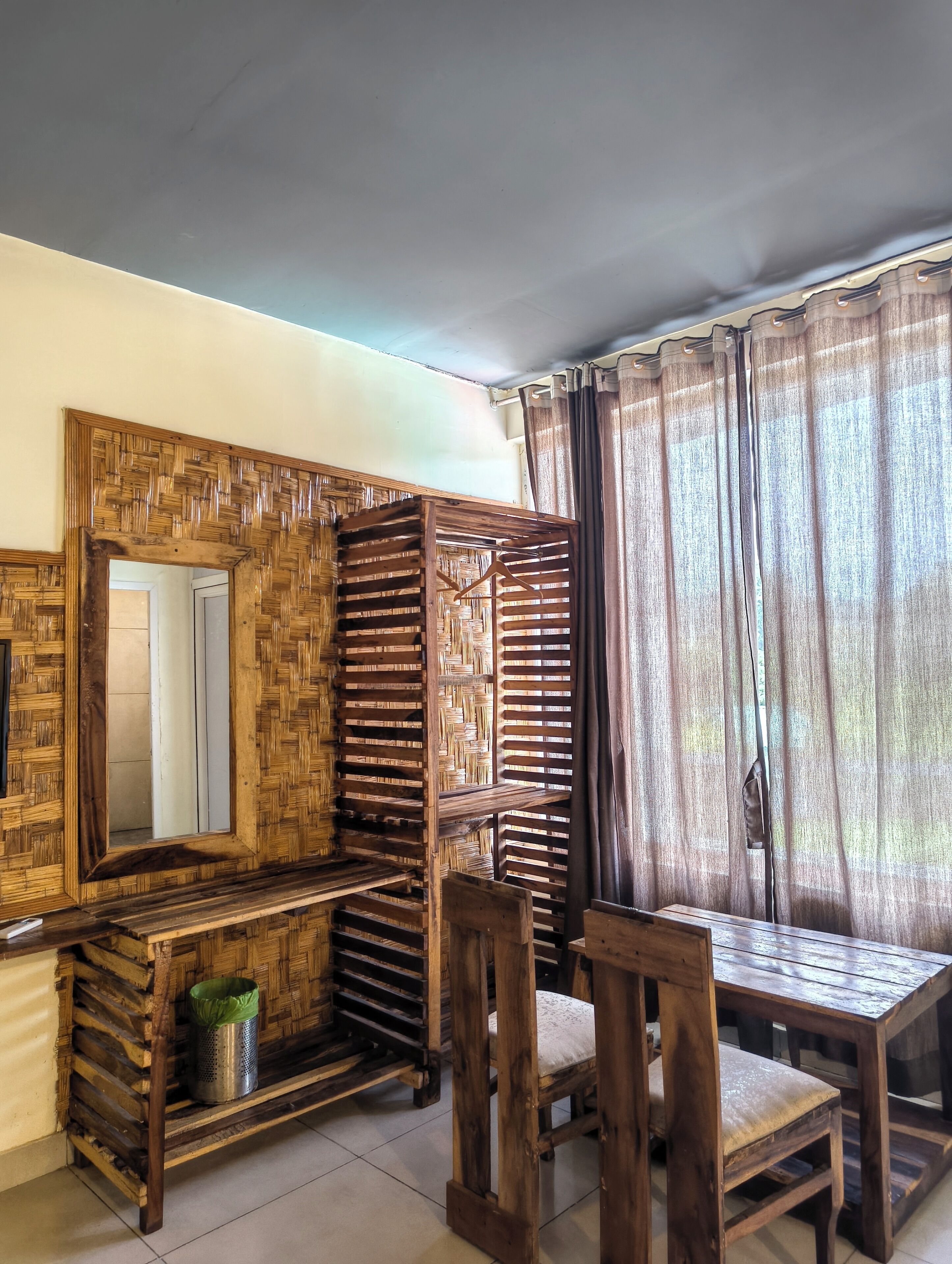 Quarto com um banco de madeira, uma mesa, um espelho e uma janela com cortinas.