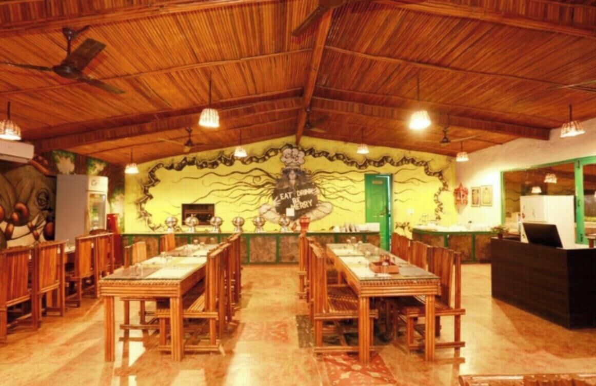 Um restaurante com mesas e cadeiras de madeira, um mural na parede e um ventilador de teto.