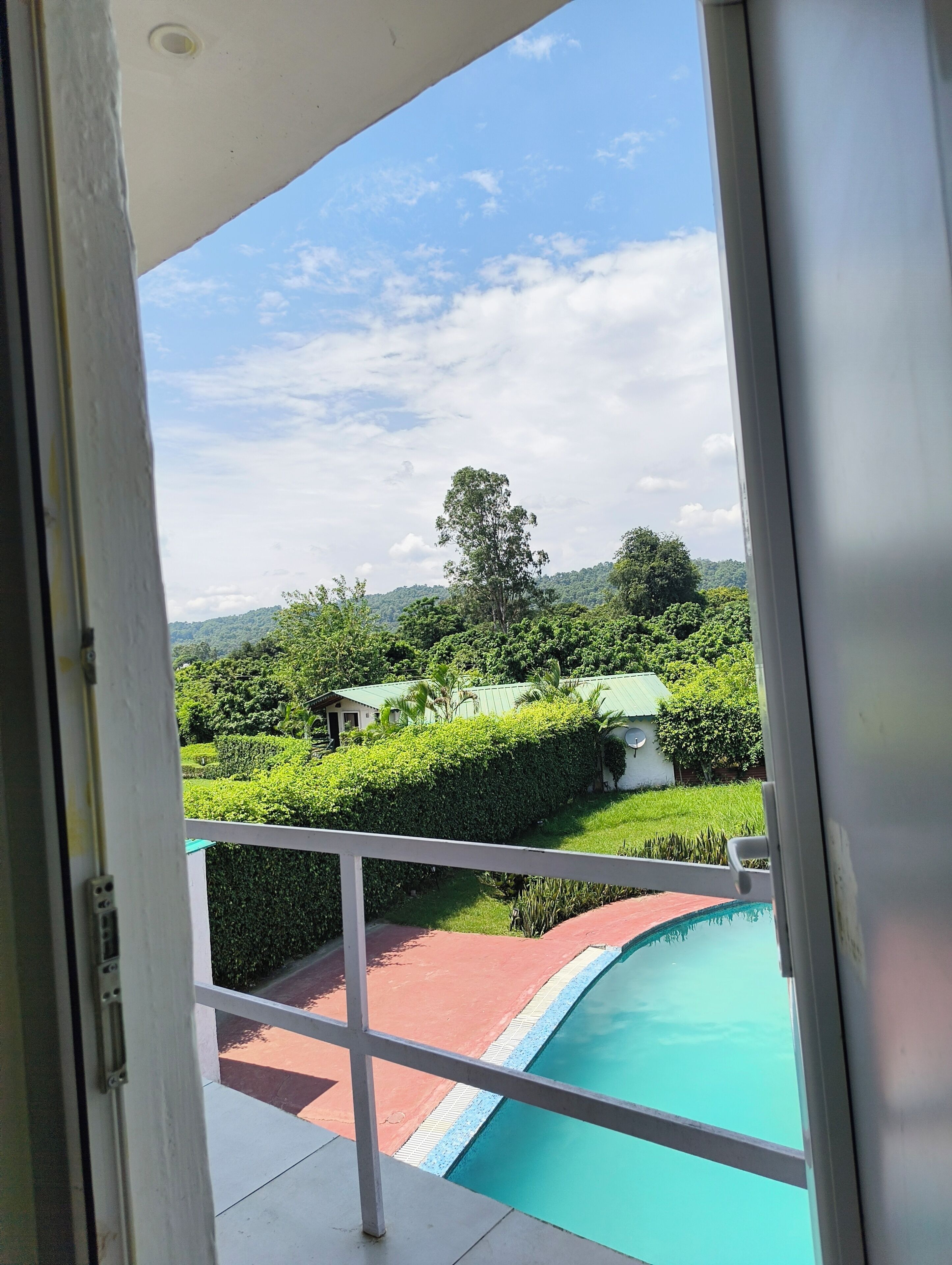 Vista de uma varanda com piscina, gramado verde e uma casa ao fundo.