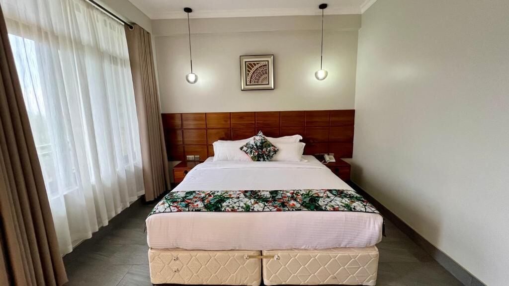 Quarto de hotel com uma cama grande, cabeceira de madeira, mesa de cabeceira e uma obra de arte pendurada na parede.