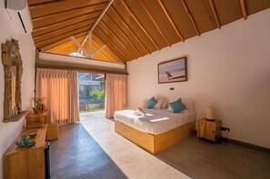 Um quarto com uma cama grande, cabeceira de madeira, um quadro de uma paisagem costeira e vista para um jardim pela janela.