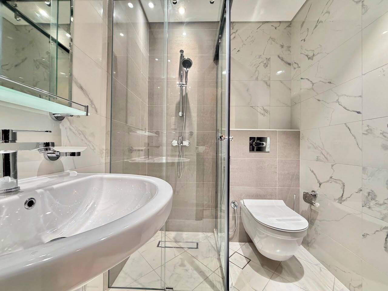 Uma casa de banho moderna com chuveiro em cabine de vidro, uma grande pia branca e uma sanita.