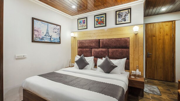 Quarto com cabeceira de madeira, cama com roupa de cama branca e duas almofadas, mesa de cabeceira e guarda-roupa de madeira.