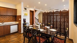 Uma área de jantar com uma mesa de madeira posta para quatro pessoas, rodeada por cadeiras com almofadas estampadas.
