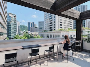 Terraço no telhado com área de bar, assentos e vista da paisagem urbana.