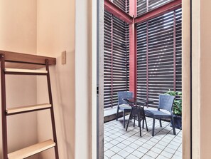 Quarto com janela de estrutura metálica, escada de madeira e uma pequena mesa com cadeiras.