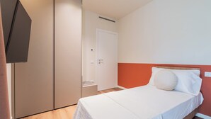 A hotel room with a bed, a wardrobe, a door, and a wall-mounted air conditioning unit.