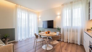 A modern living room with a dining area, wooden flooring, and a flat-screen TV mounted on the wall.