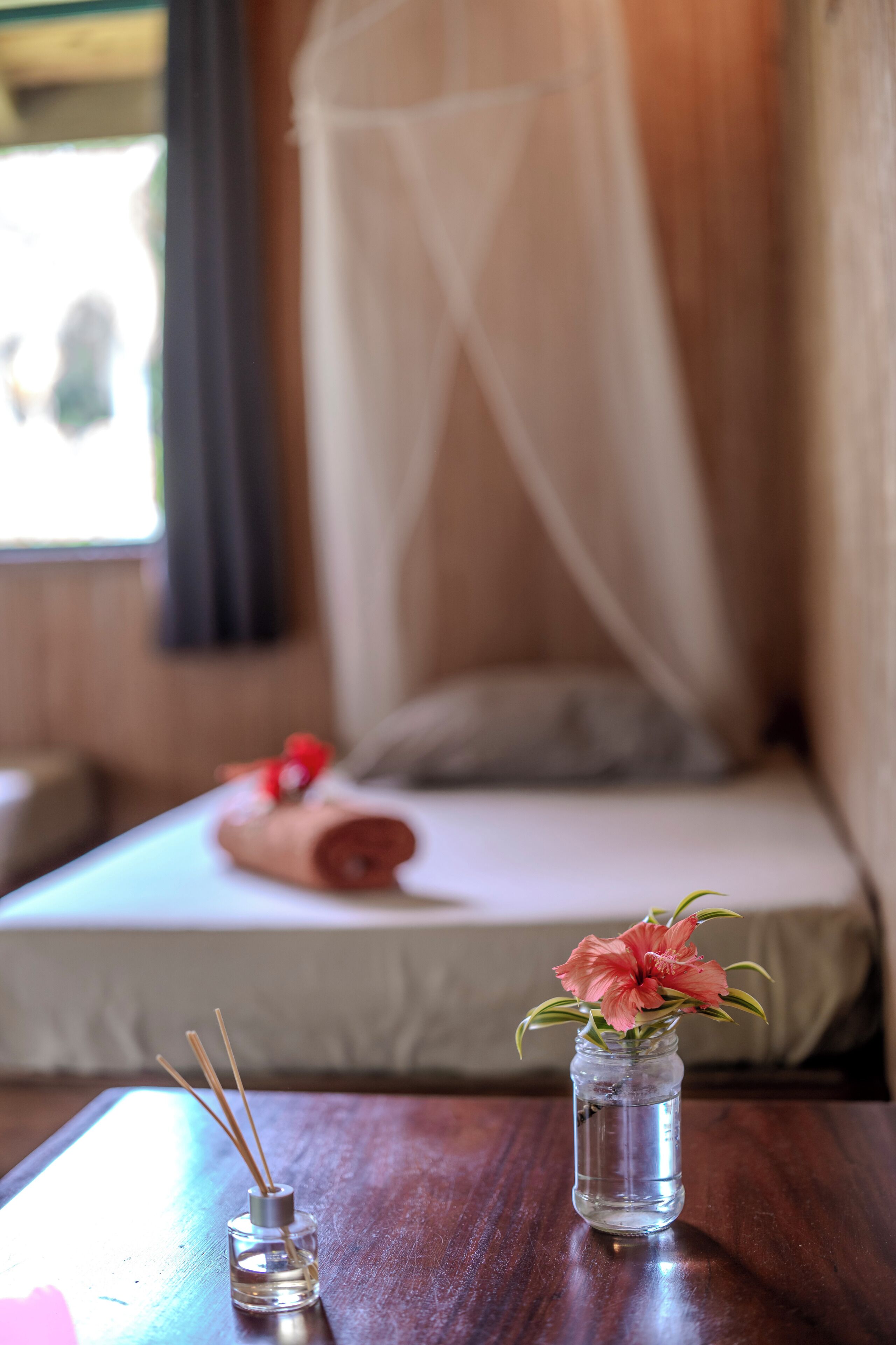 Um quarto com uma cama, uma mesinha com um vaso de flores e uma janela com cortinas.