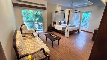 Quarto com cama de dossel, sofá, mesa de centro e janelas amplas.