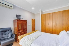 Quarto com cama, guarda-roupa de madeira, poltrona de couro e televisão sobre um móvel.