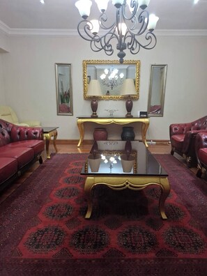 Uma sala de estar com uma mesa de centro, sofás vermelhos, um candelabro e um tapete estampado.
