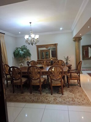 Uma sala de jantar com uma mesa grande e ricamente decorada, cadeiras combinando, um candelabro e um espelho.