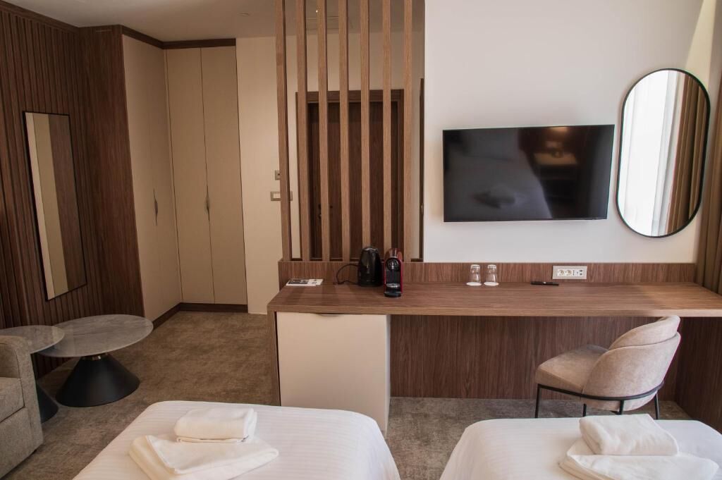 Quarto de hotel com cama, escrivaninha, cadeira, televisão e espelho.
