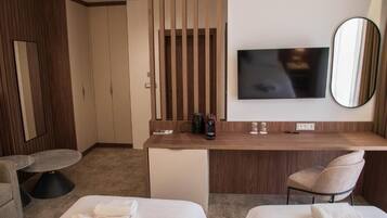 Quarto de hotel com cama, escrivaninha, cadeira, televisão e espelho.