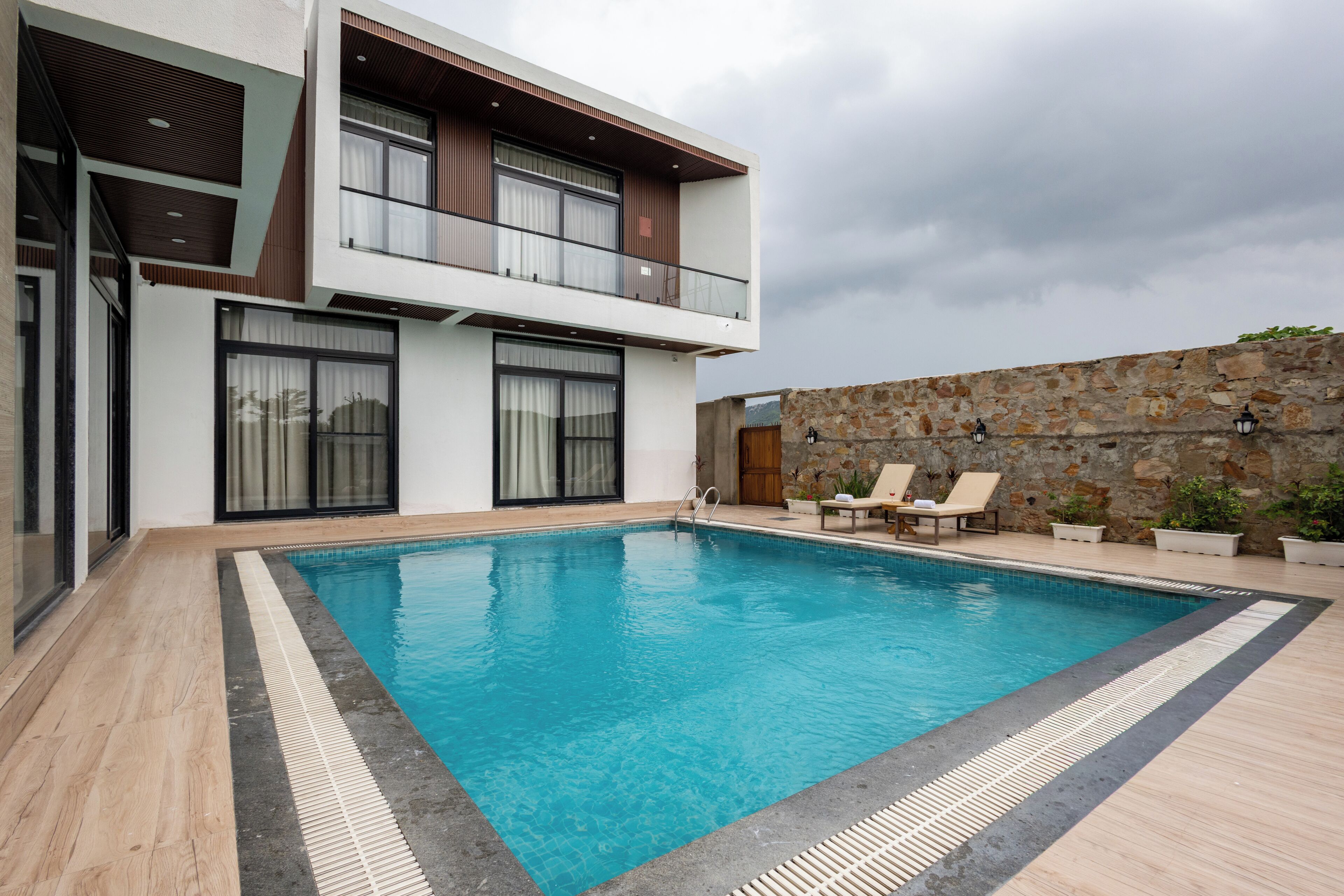 Um edifício moderno de dois andares com piscina, área de estar externa e parede de pedra.