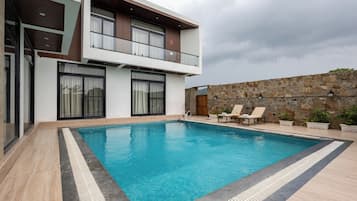 Um edifício moderno de dois andares com piscina, área de estar externa e parede de pedra.