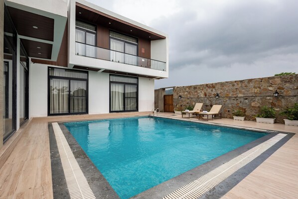 Um edifício moderno de dois andares com piscina, área de estar externa e parede de pedra.