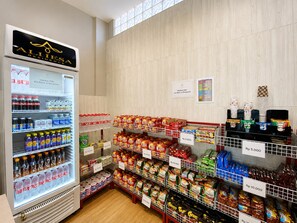 Um dispensador de bebidas refrigeradas e prateleiras repletas de lanches e condimentos.