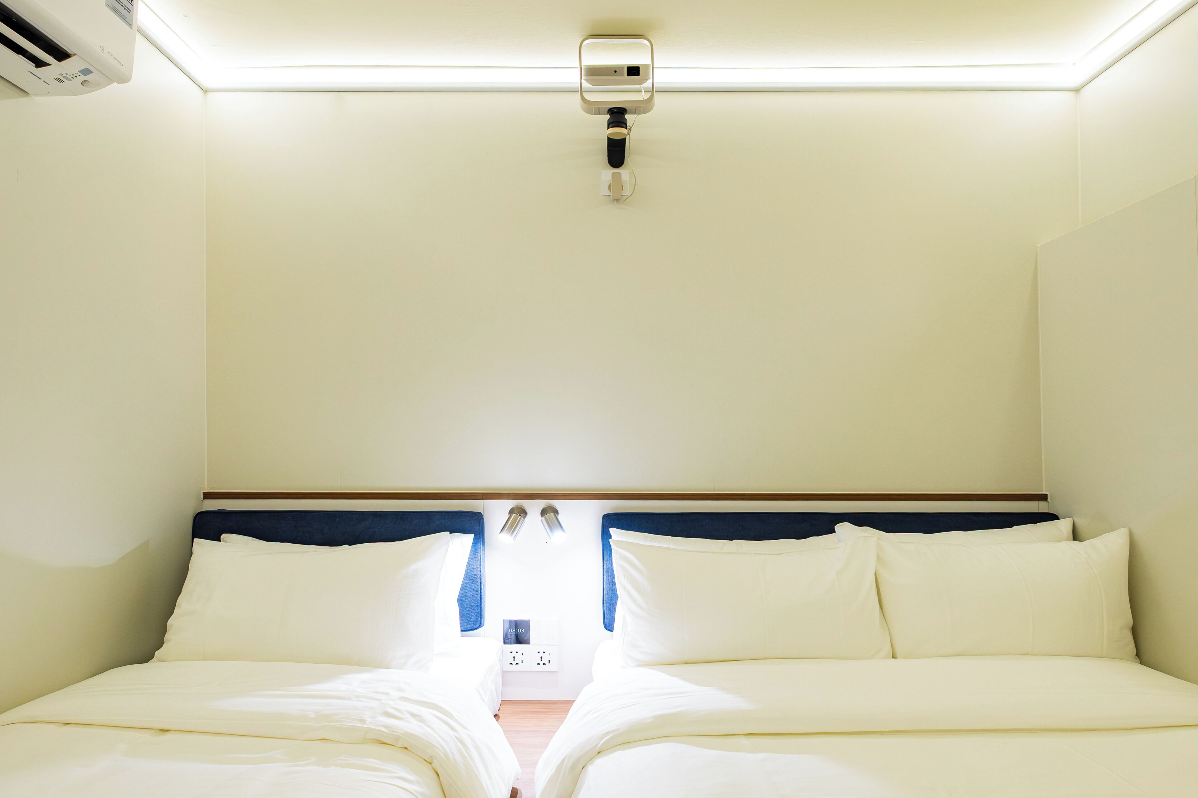 Quarto de hotel com cama, mesa de cabeceira, ar condicionado fixado na parede e uma tomada.