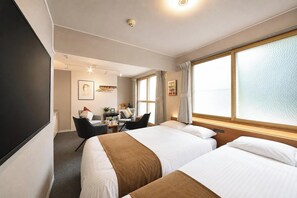 Quarto de hotel com duas camas, uma escrivaninha, uma cadeira e uma janela grande.